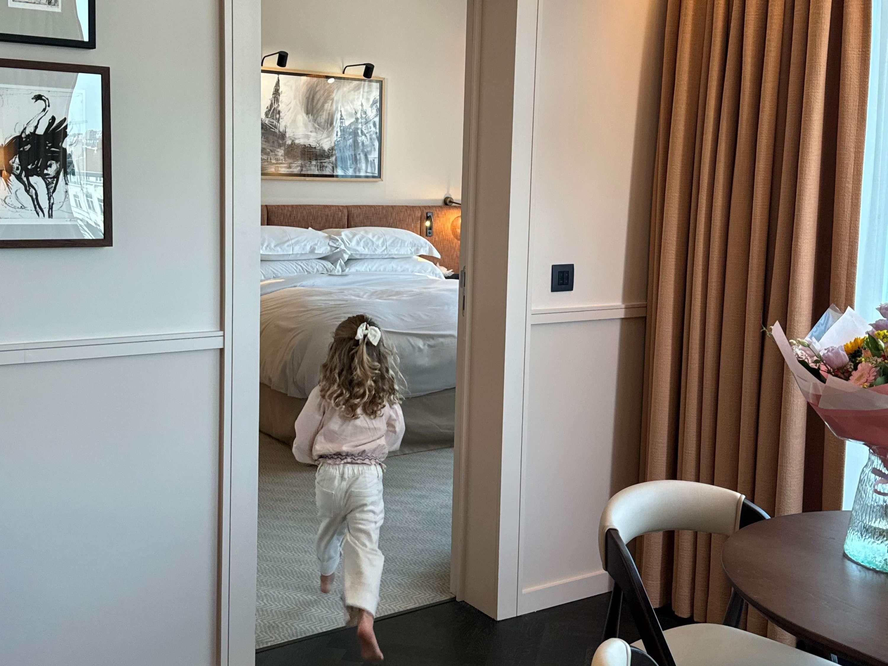 Quarto de hotel com cama, um quadro na parede, cortina e mesa com um vaso de flores.