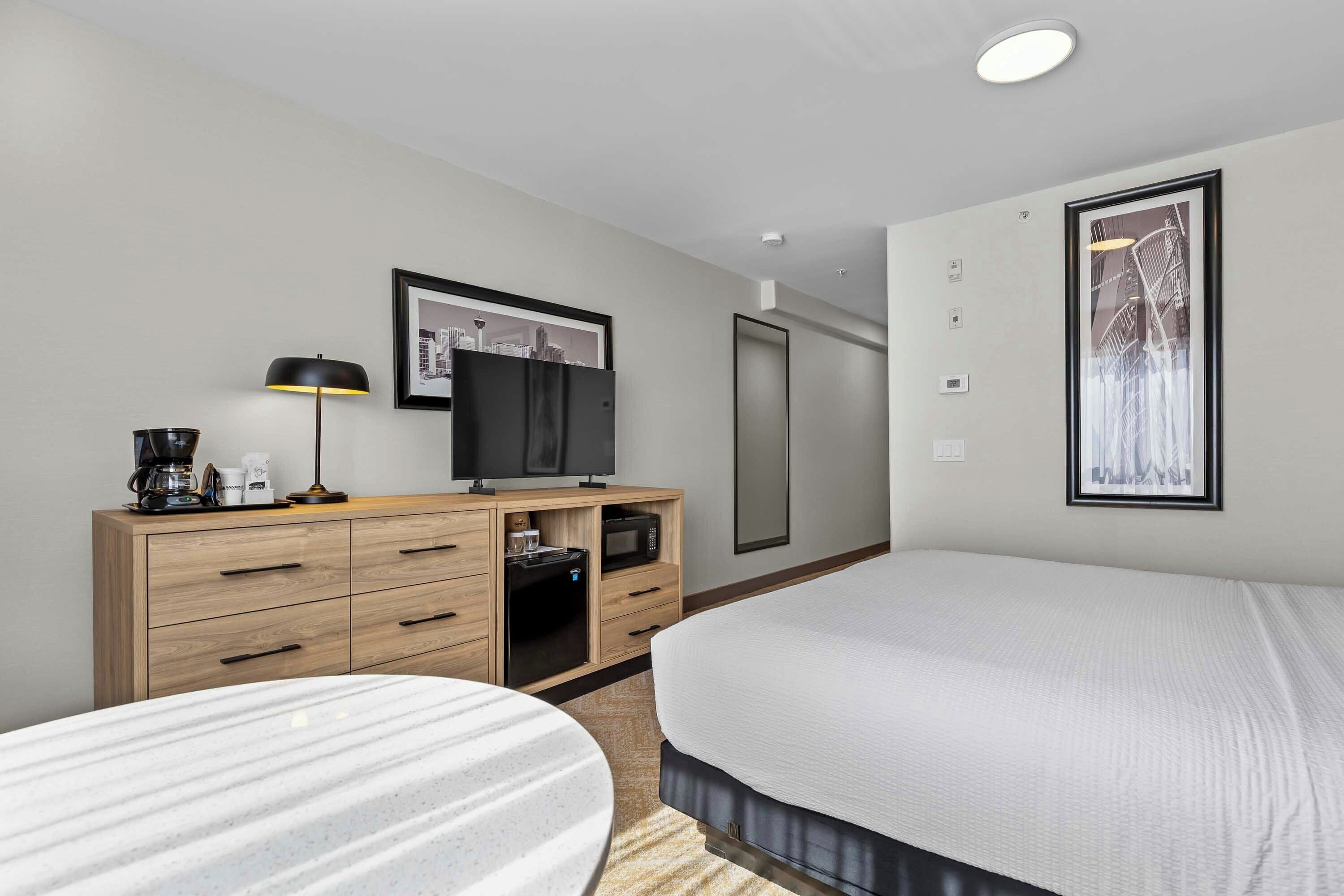 Quarto de hotel com duas camas, televisão, máquina de café, abajur e um quadro na parede.