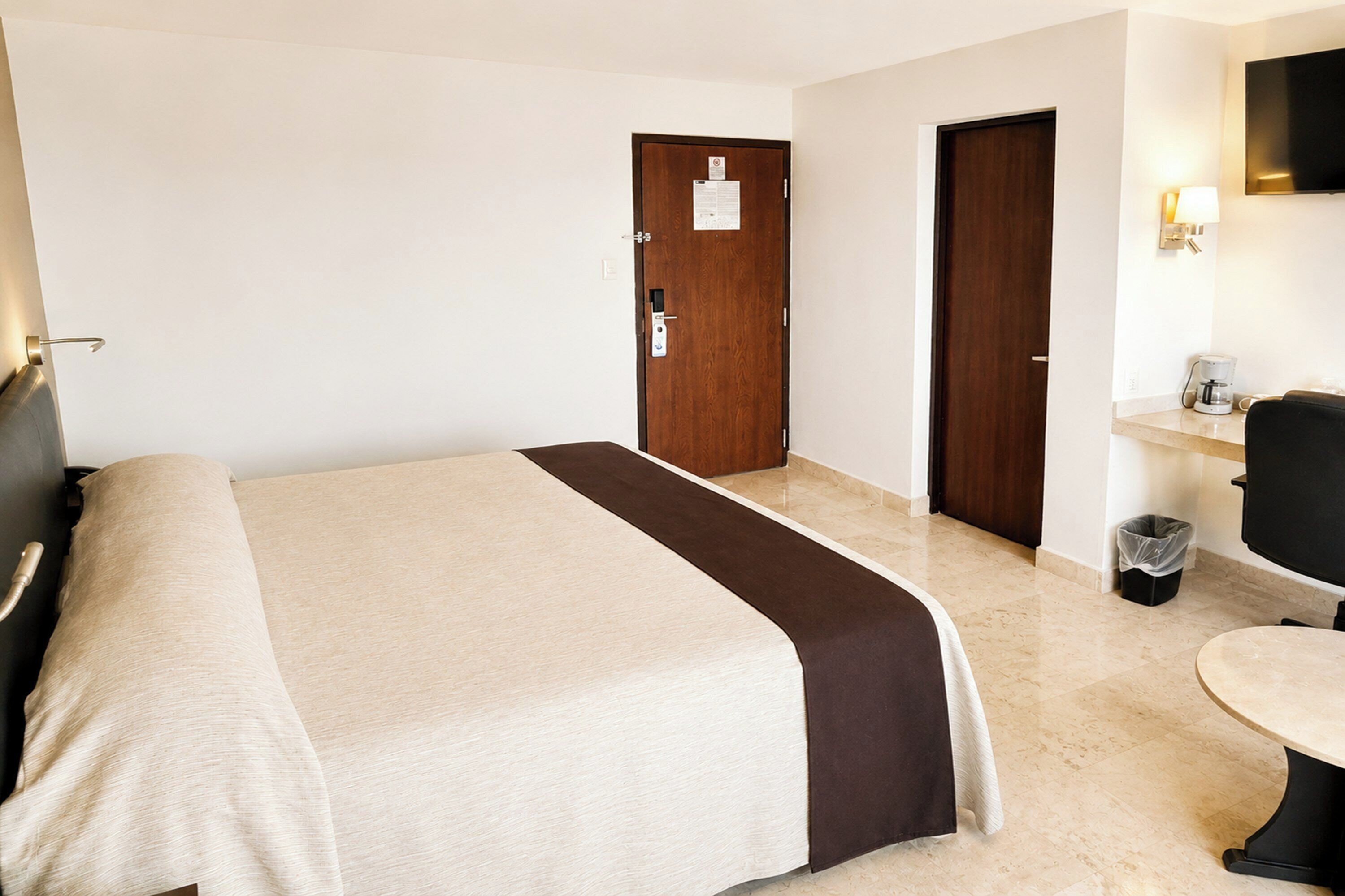 Quarto de hotel com cama, escrivaninha, cadeira, televisão e máquina de café.