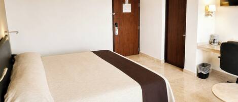 Quarto de hotel com cama, escrivaninha, cadeira, televisão e máquina de café.