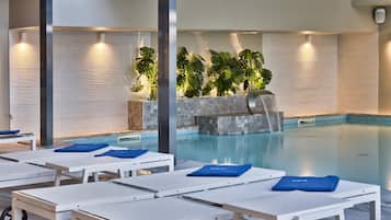 Uma área junto à piscina com espreguiçadeiras, uma cascata e plantas em vasos.