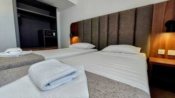 Quarto de hotel com duas camas, um guarda-roupa, uma escrivaninha e uma televisão.