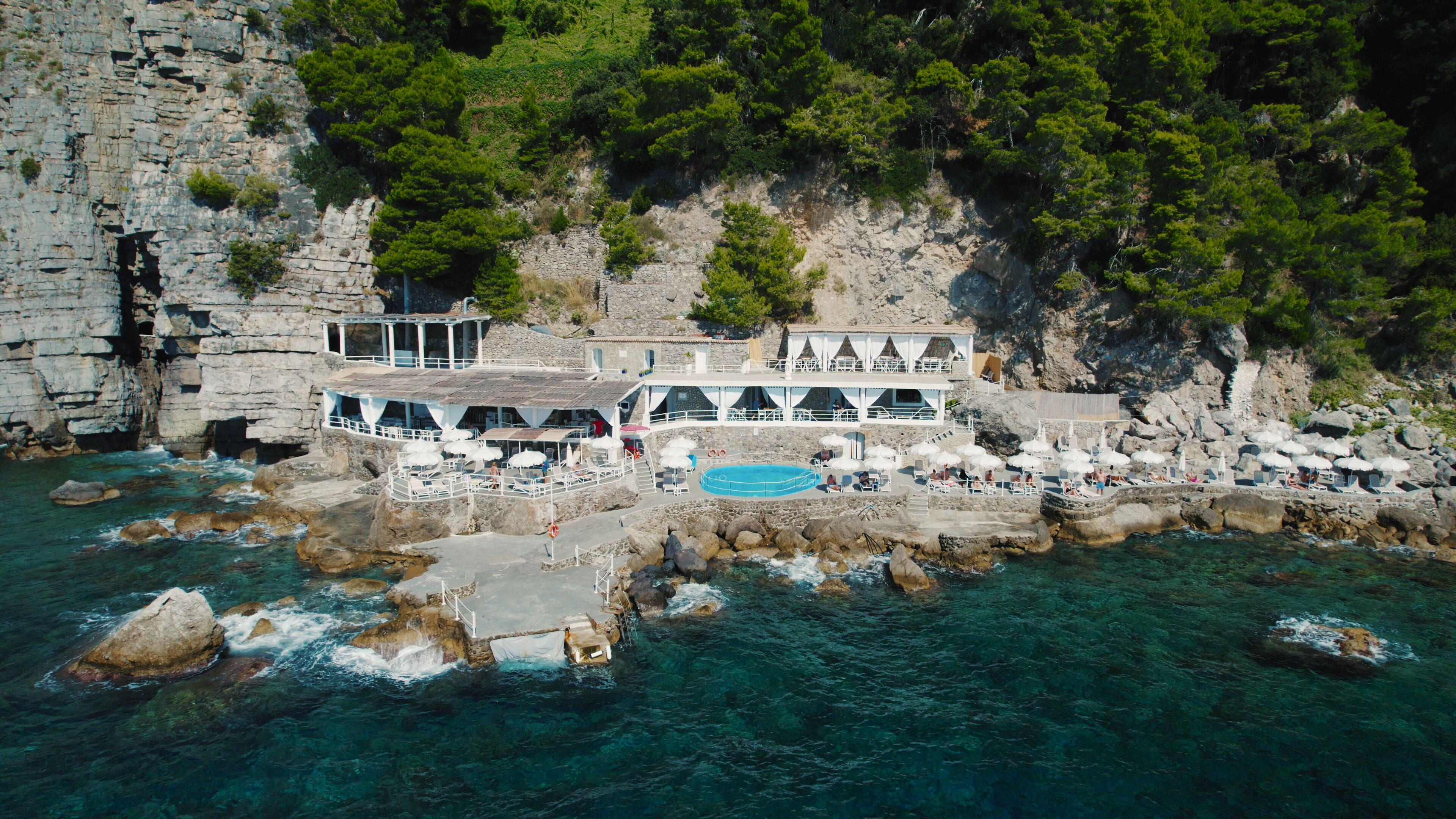 Um hotel à beira-mar com piscina, área externa para sentar e vista para o mar.