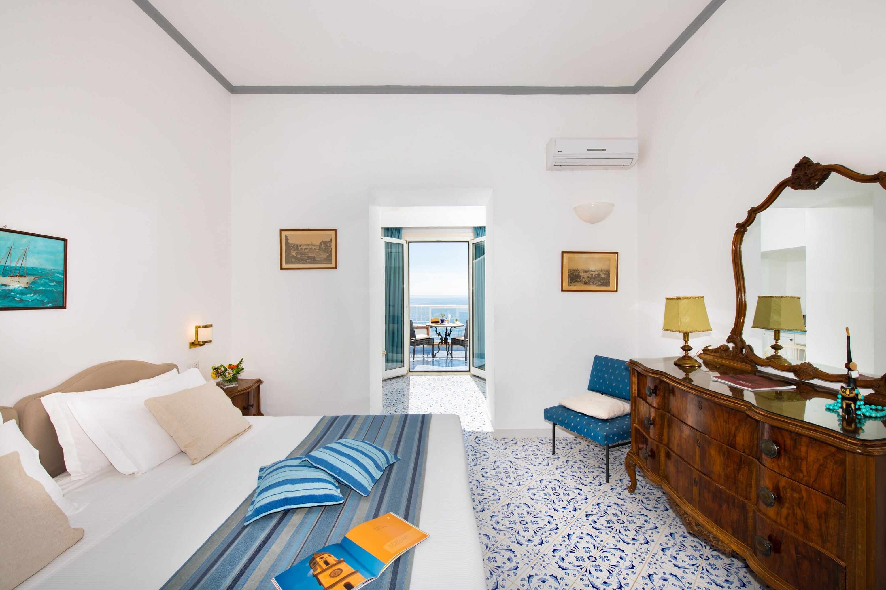 Quarto de hotel com cama, penteadeira e vista para o mar através de uma porta de vidro.