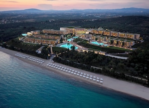 Um resort com vários edifícios, uma piscina e uma praia com espreguiçadeiras.