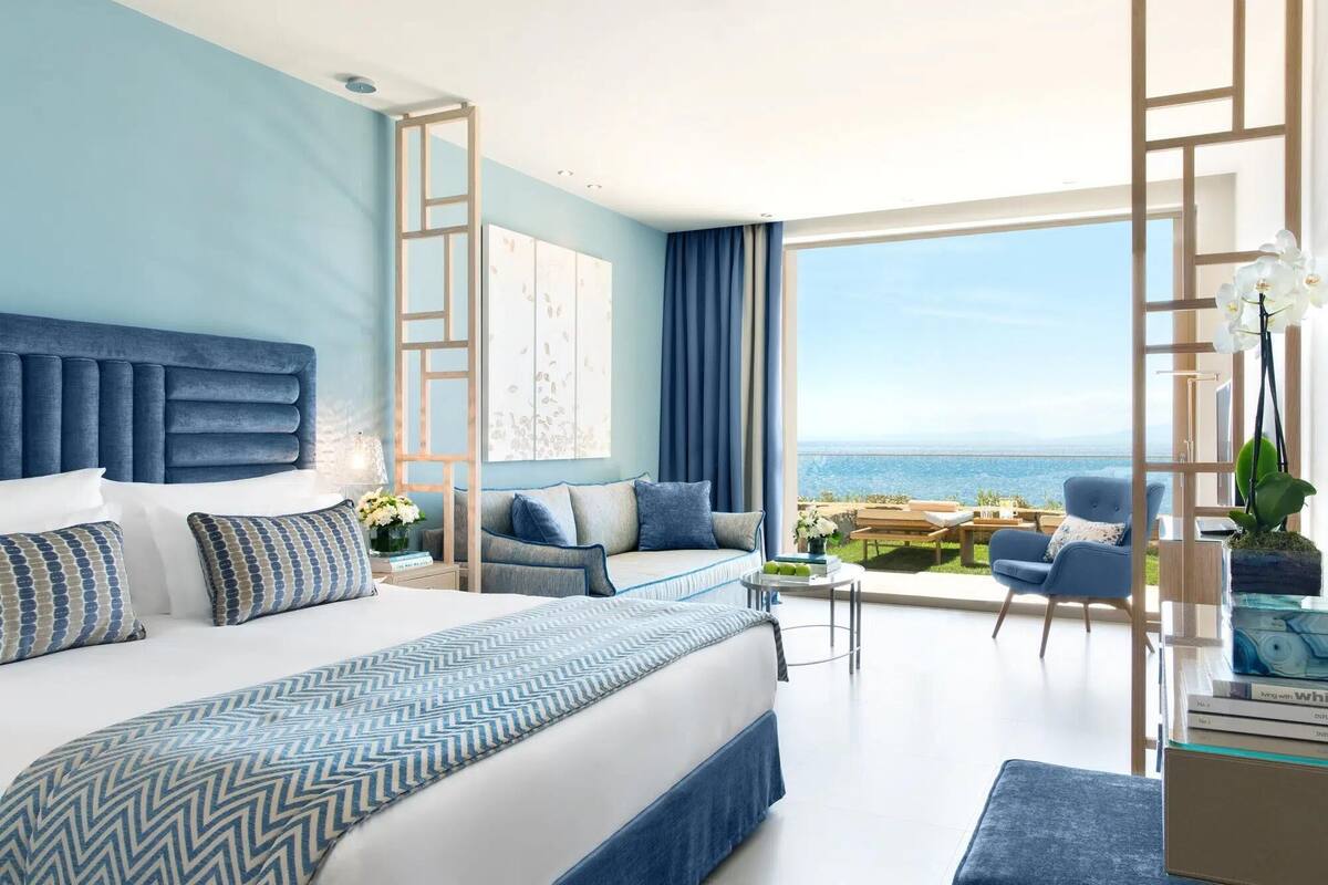 Quarto moderno com uma cama grande, um sofá e uma varanda com vista para o mar.