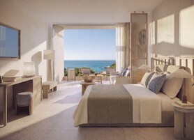 Quarto moderno com uma cama grande, uma escrivaninha e vista para o mar.