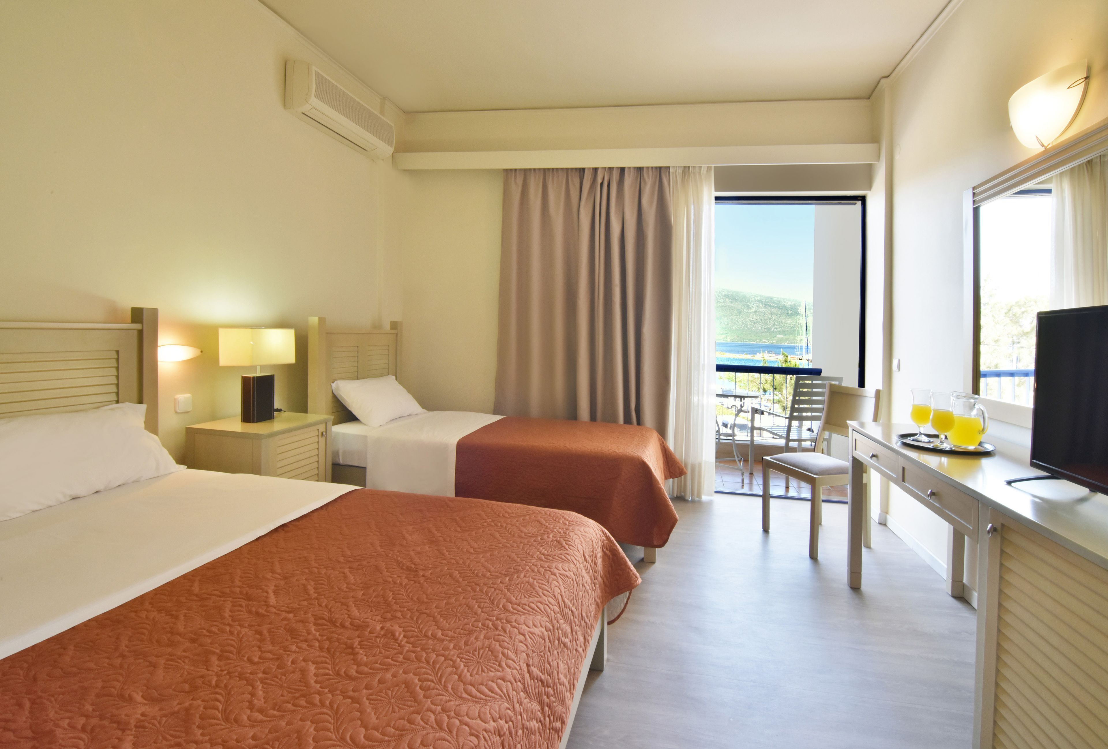 Quarto de hotel com duas camas, uma escrivaninha com cadeira, televisão e janela com vista para o exterior.