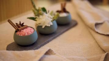 Três pequenas tigelas em um suporte, cada uma contendo cristais cor-de-rosa e um pau de canela, com uma flor branca em uma delas.