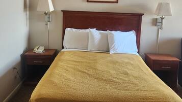 Quarto de hotel com uma cama grande, duas mesas de cabeceira com luminárias, um quadro na parede e um telefone em uma das mesas.