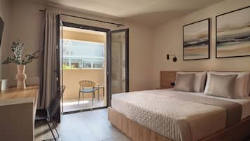 Quarto de hotel com cama, uma cadeira, uma mesa, uma planta em vaso e varanda com vista.