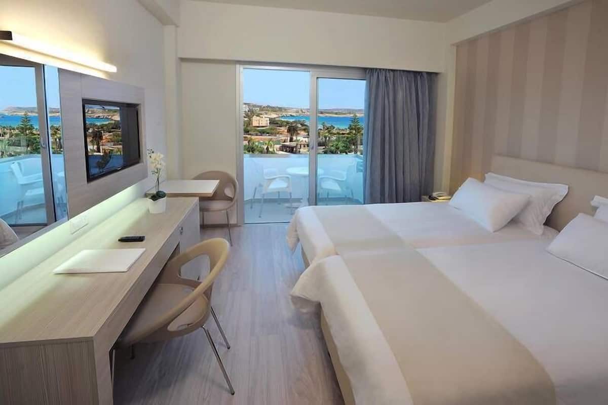 Quarto de hotel com cama, escrivaninha, cadeira e televisão.