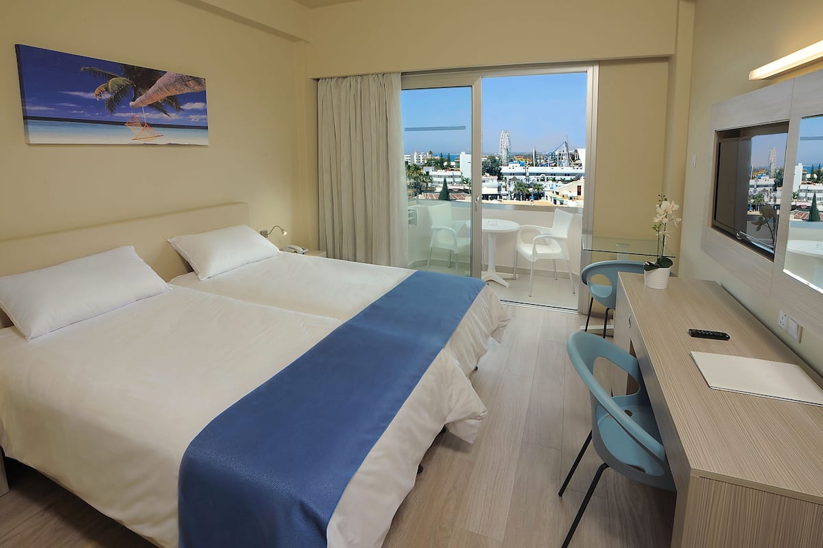 Quarto de hotel com duas camas, uma escrivaninha e vista para a cidade.