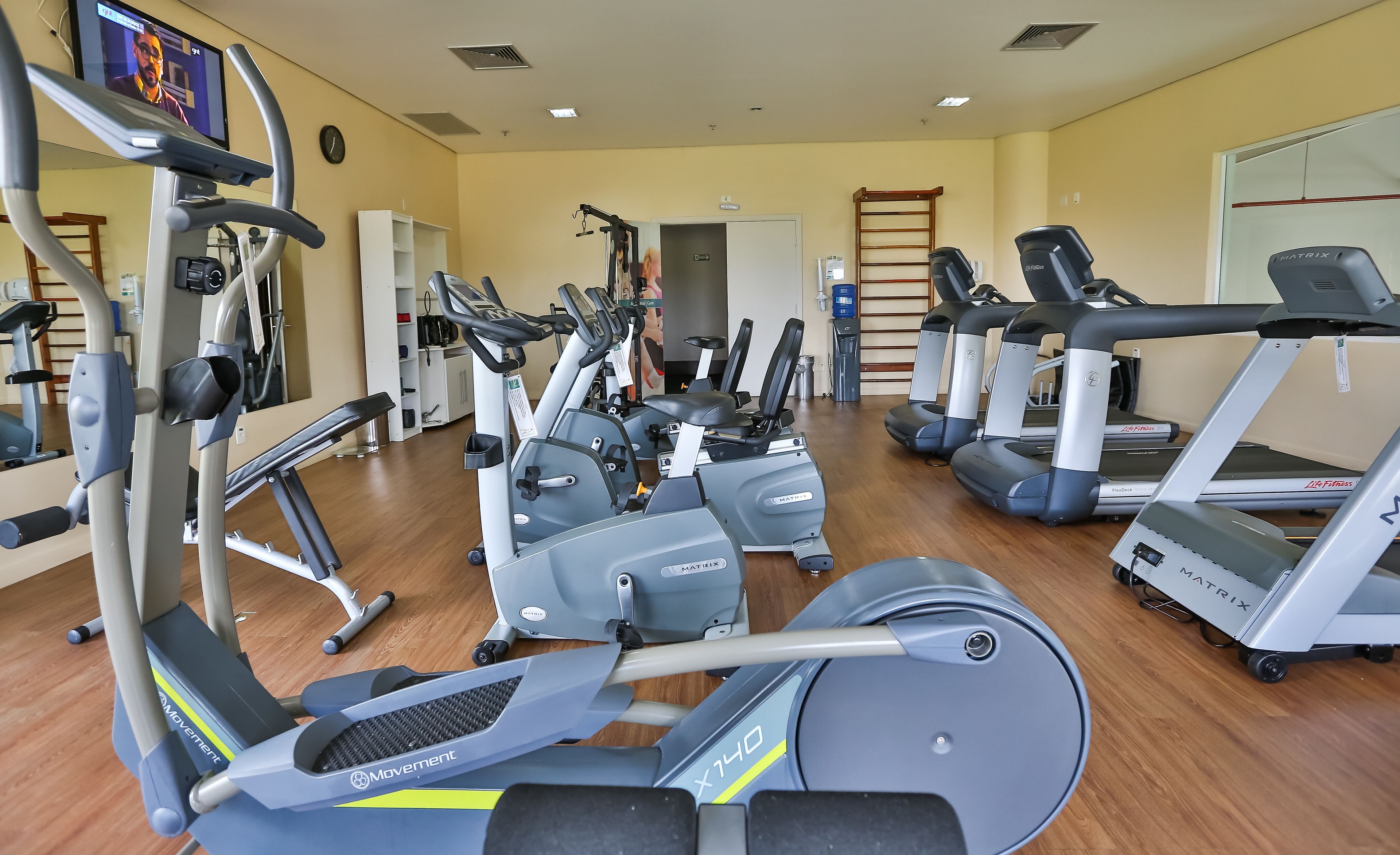 Uma academia com diversos equipamentos de ginástica cardiovascular, incluindo esteiras e elípticos.
