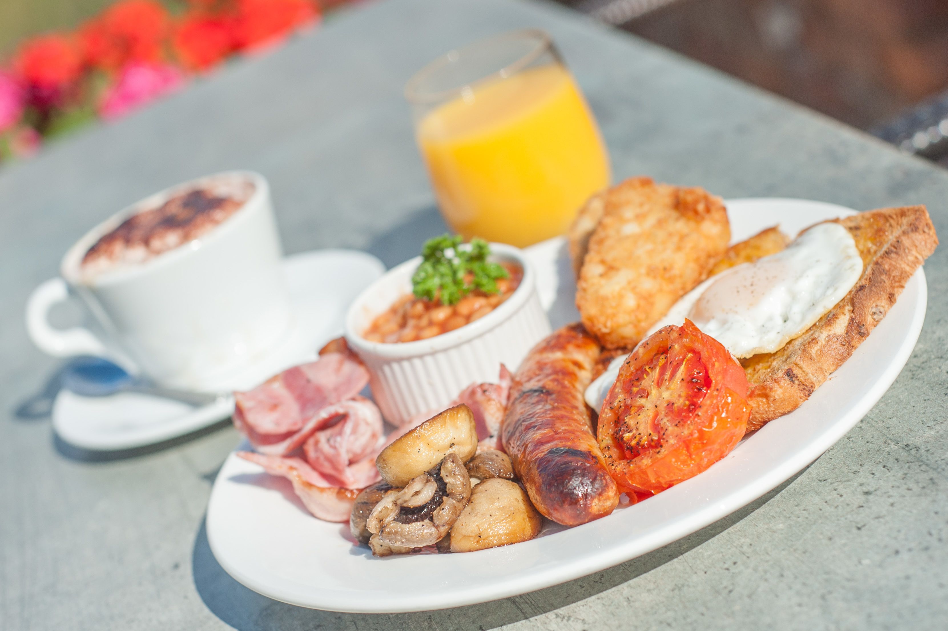 Prato de café da manhã com ovos, linguiça, cogumelos e tomates, acompanhado de um copo de suco de laranja e uma xícara de café.
