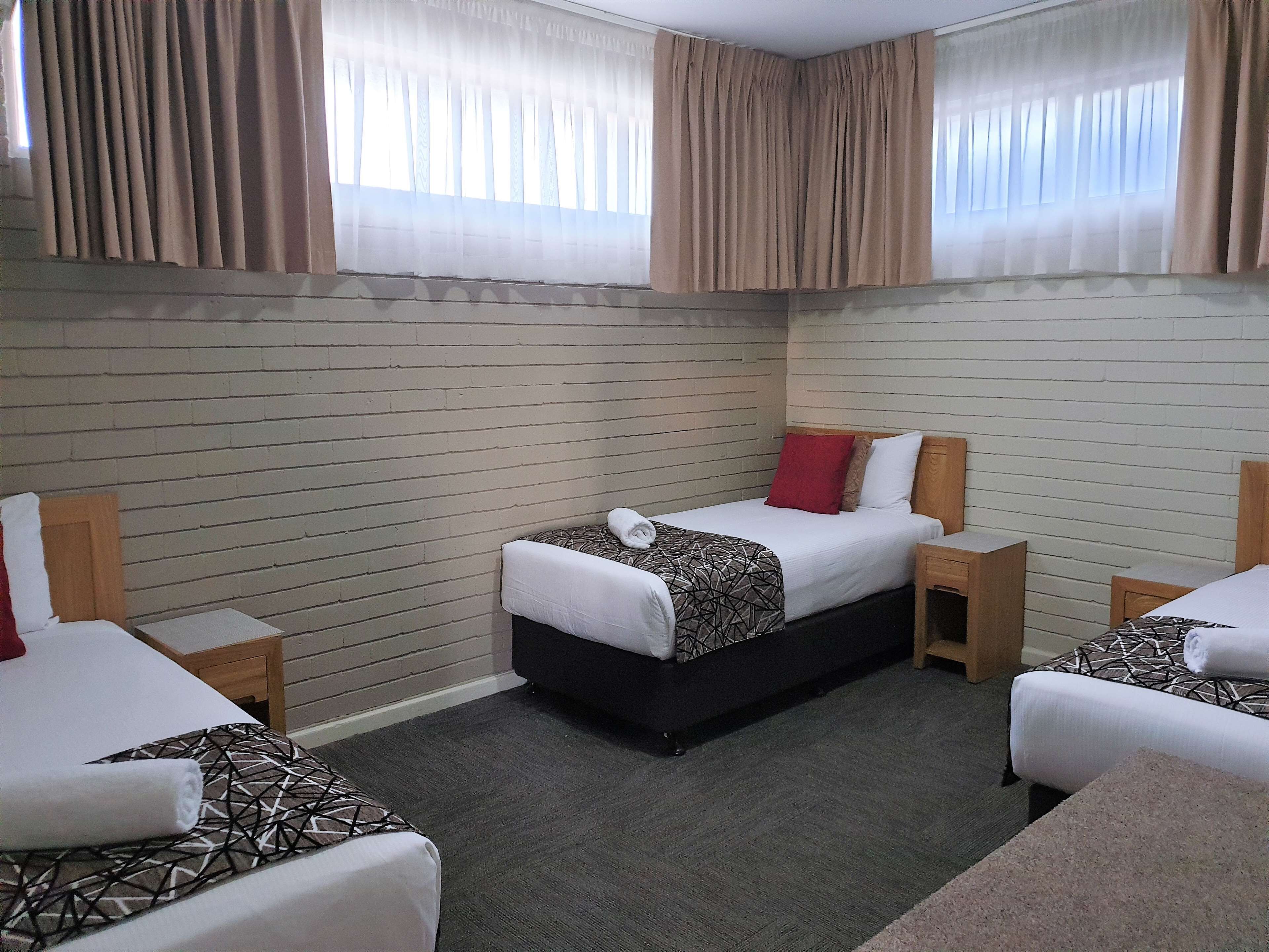 Quarto de hotel com duas camas, cabeceira de madeira, mesa de cabeceira pequena e janela com cortinas.