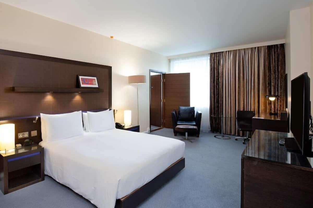 Quarto de hotel com cama, mesas de cabeceira, escrivaninha, cadeira e televisão.