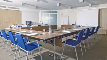Uma sala de conferências com uma mesa comprida, cadeiras azuis e um quadro branco.