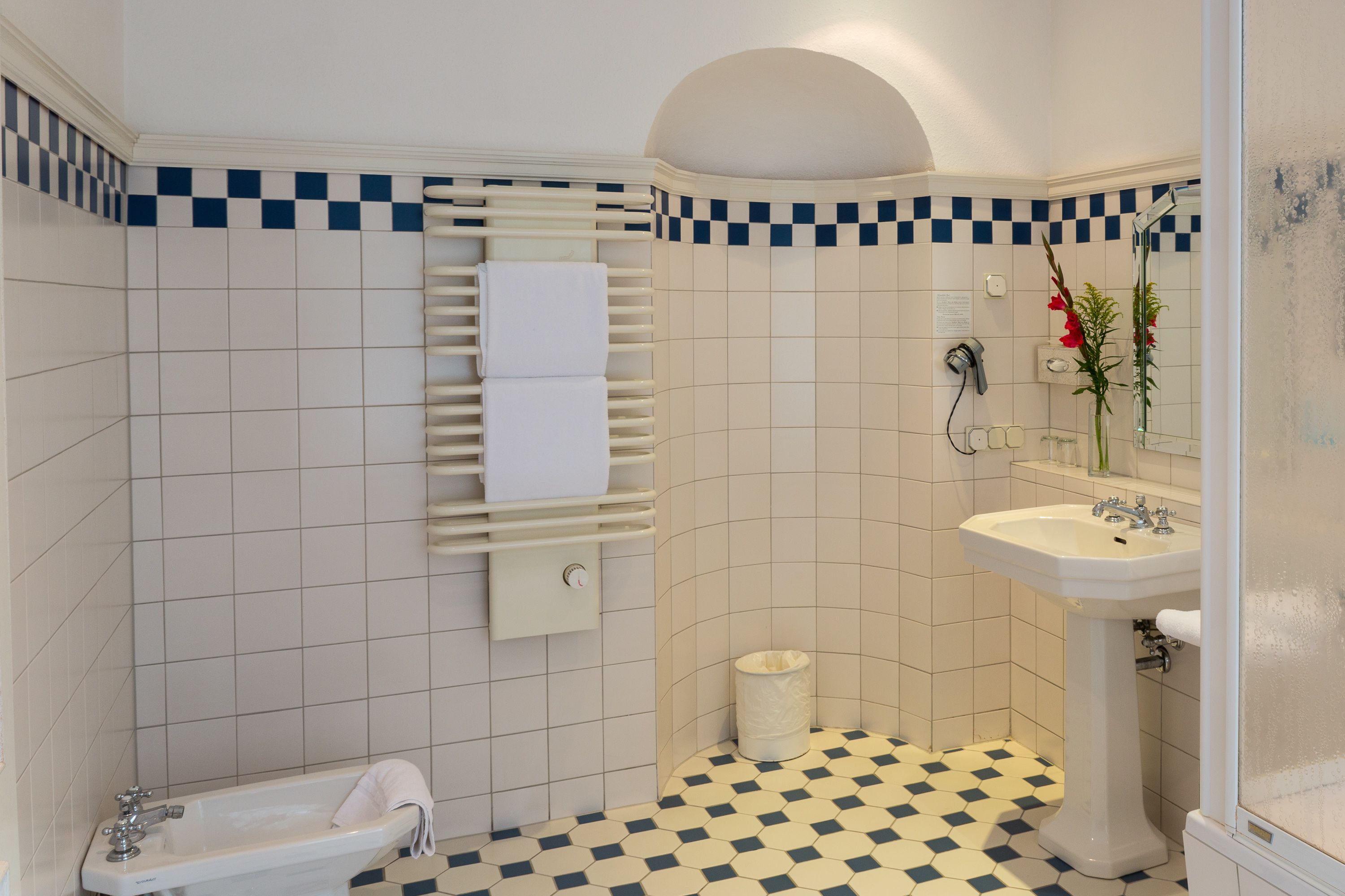 Um banheiro com piso xadrez, pia, espelho, porta-toalhas e vaso sanitário.