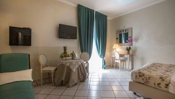 Quarto de hotel com cama, escrivaninha com cadeira, televisão na parede e janela com cortinas.