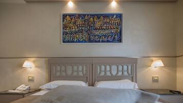Quarto de hotel com cama, duas luminárias de cabeceira, um telefone na mesinha de apoio e um quadro na parede.