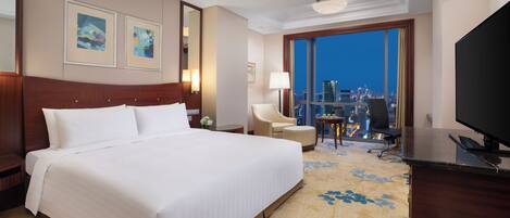 Quarto de hotel com uma cama grande, uma mesa, uma cadeira, uma TV e vista para a cidade.