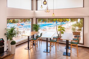 Uma área de refeições moderna em ambiente interno, com grandes janelas que dão para uma piscina e área de estar externa.