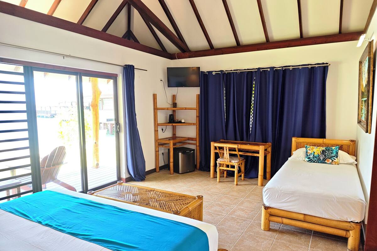 Quarto com duas camas, uma escrivaninha, uma cadeira, televisão e porta de correr para o exterior.