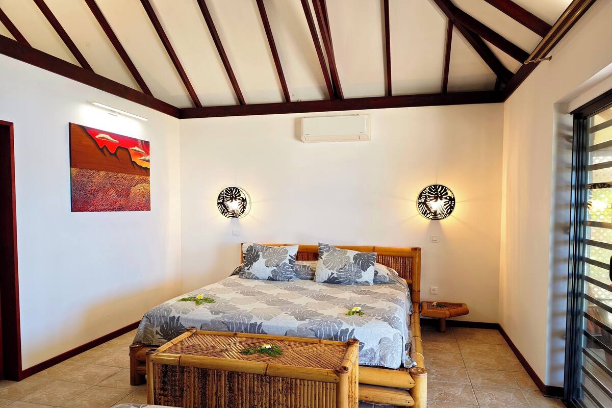 Quarto com cama, mesa de cabeceira, luminária na parede e janela com persianas.