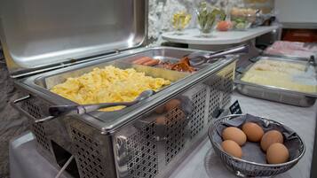 Buffet com diversos alimentos, incluindo ovos mexidos, salsichas e ovos em uma tigela.