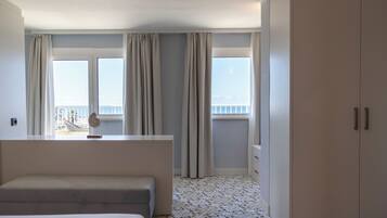Quarto de hotel com cama, escrivaninha, armário e amplas janelas com cortinas.