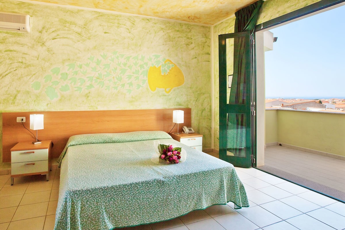 Quarto de hotel com cama, mesas de cabeceira, decoração na parede e varanda com vista.
