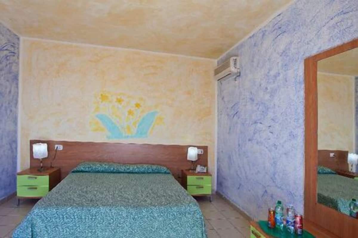 Quarto de hotel com cama, duas mesas de cabeceira, um espelho e uma parede com uma pintura floral.