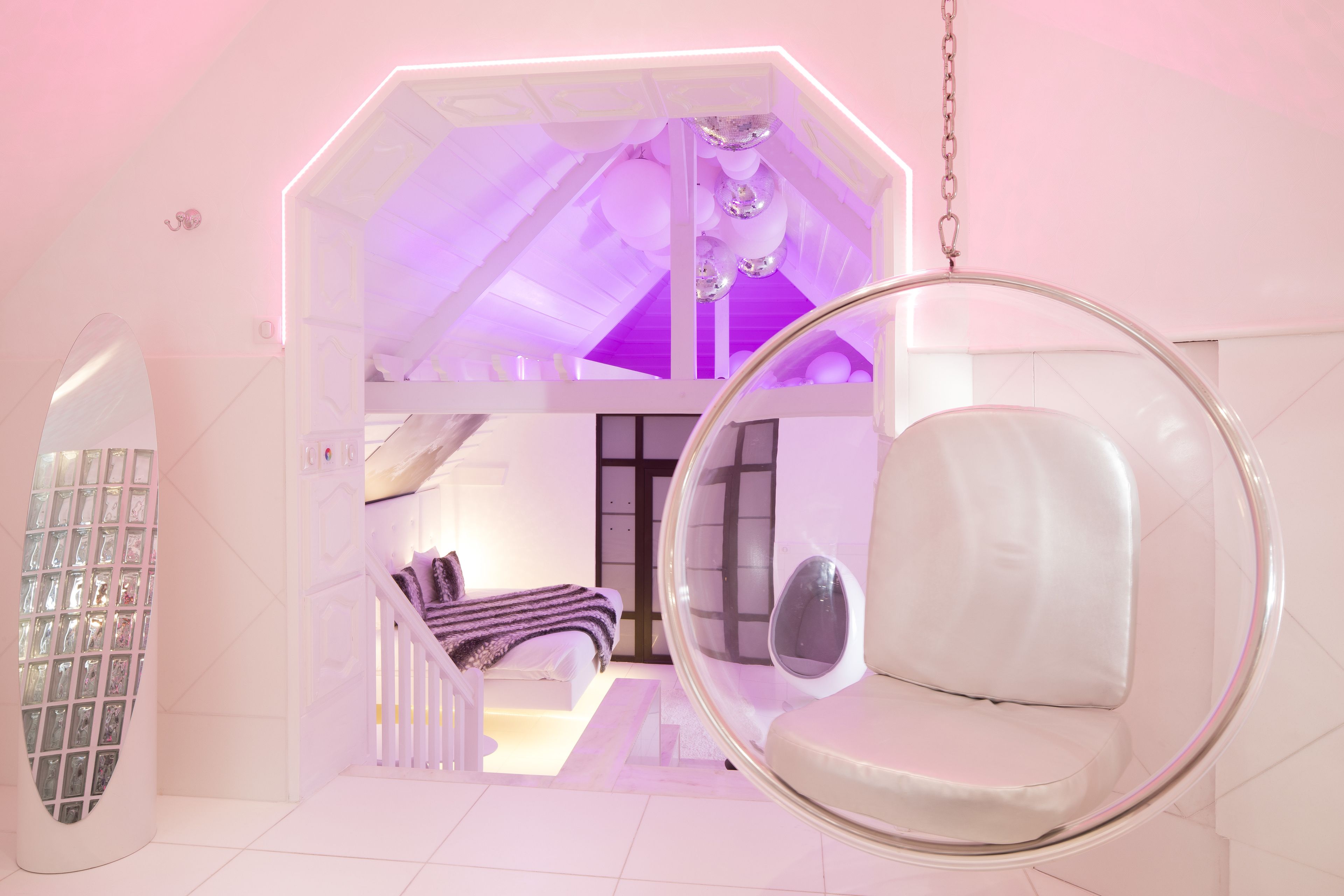 Um interior moderno com uma cadeira suspensa, um aparador de vidro e uma escada que leva a um quarto.