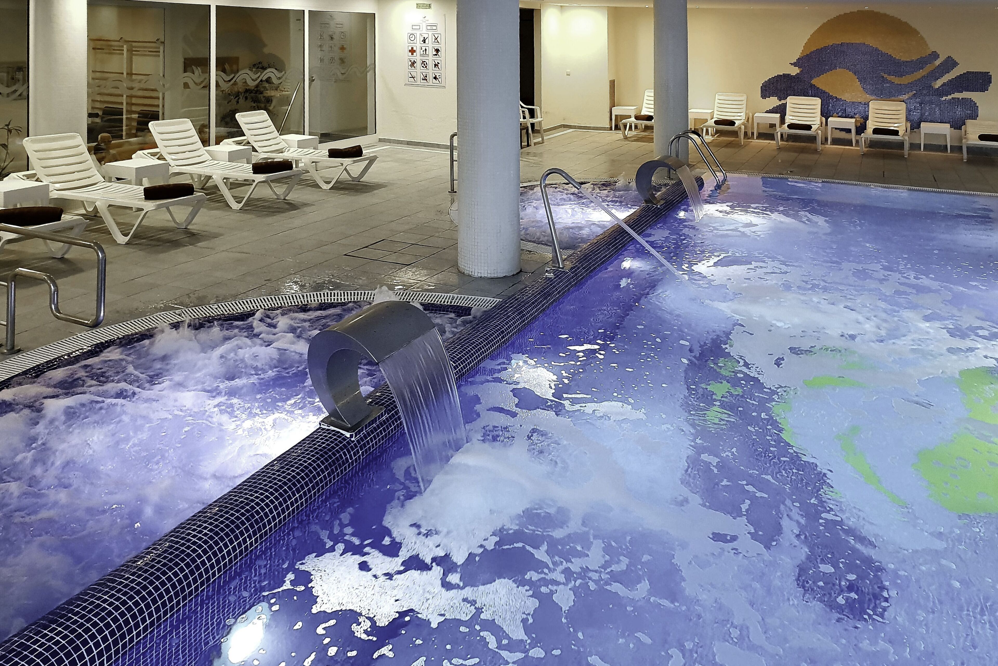 Área de piscina com espreguiçadeiras e um recurso de água.