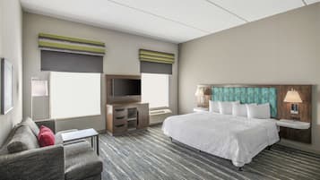 Quarto de hotel com cama, sofá, televisão e escrivaninha.