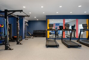 Uma academia com esteiras, máquinas de musculação e halteres.