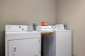 Uma área de lavanderia com uma máquina de lavar e secadora Whirlpool, uma caixa de detergente Bounce e uma toalha branca na secadora.