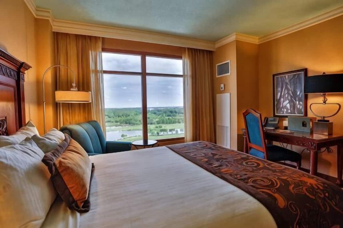 Quarto de hotel com uma cama grande, uma escrivaninha com computador, uma cadeira e vista para a paisagem.