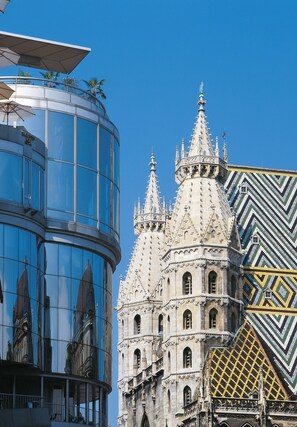 Um edifício moderno com fachada de vidro curva e um edifício tradicional com torres ornamentadas e telhas padronizadas.