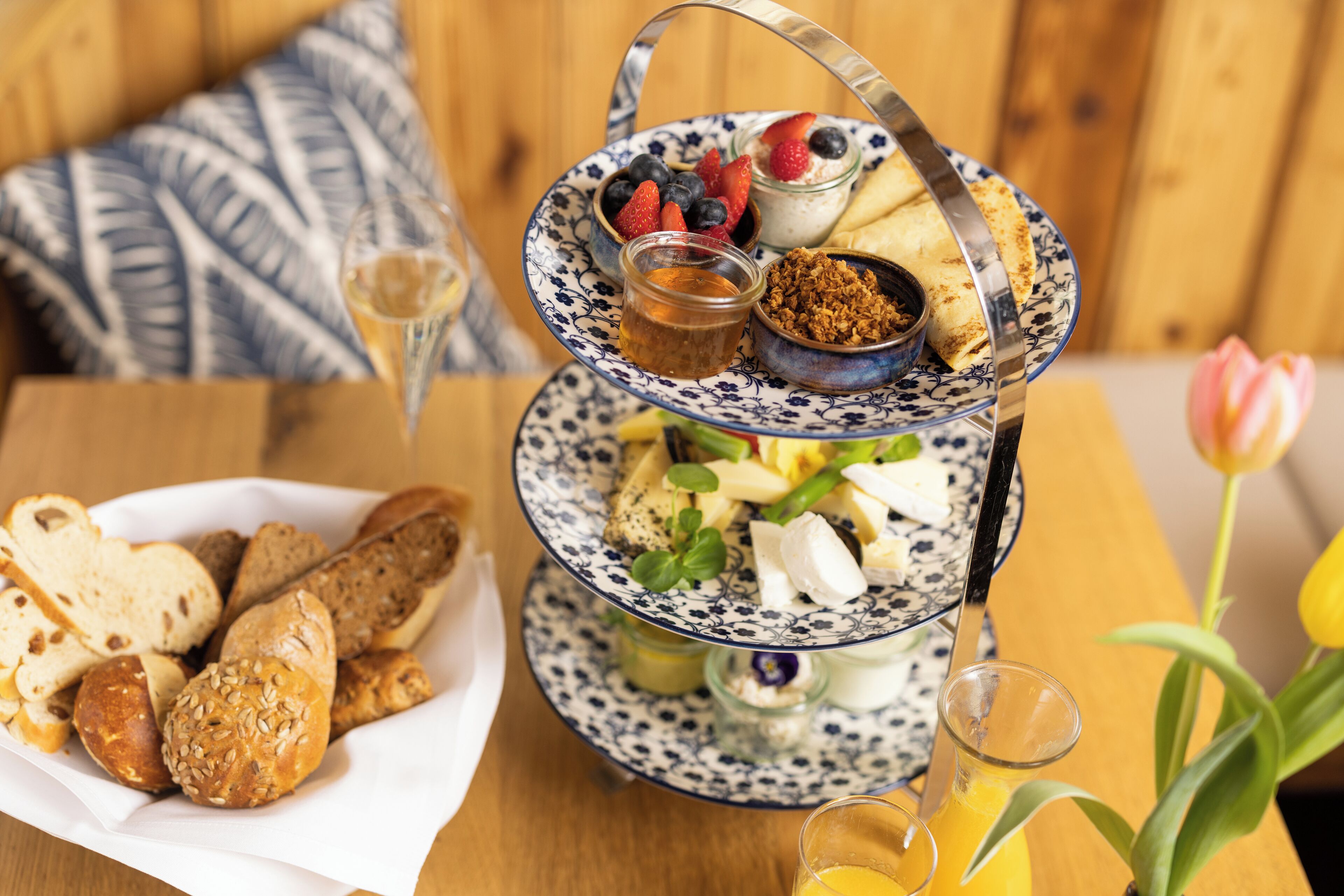 Bandeja de três níveis com diversos alimentos, um copo de suco de laranja e uma pequena tigela de granola.