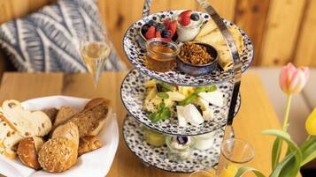 Bandeja de três níveis com diversos alimentos, um copo de suco de laranja e uma pequena tigela de granola.