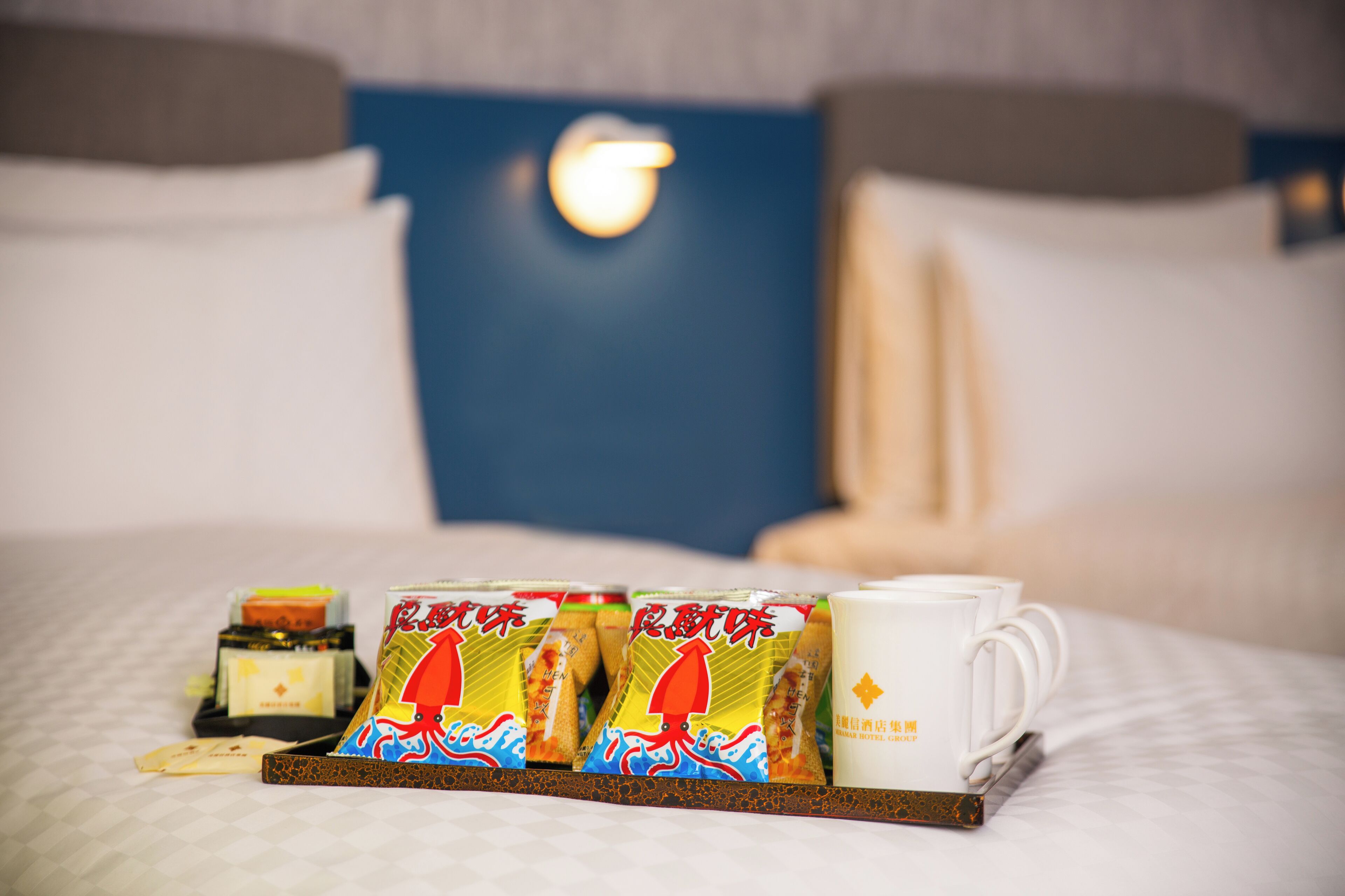 Uma cama com uma bandeja de comidas e uma caneca branca.