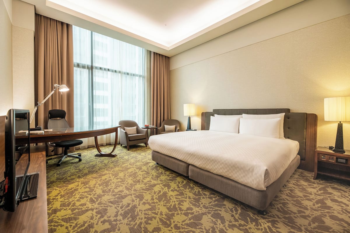 Quarto de hotel com uma cama grande, uma escrivaninha com cadeira, um computador e uma luminária.