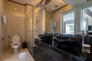 Uma casa de banho moderna com cabine de duche em vidro, sanita branca e lavatório preto suspenso.