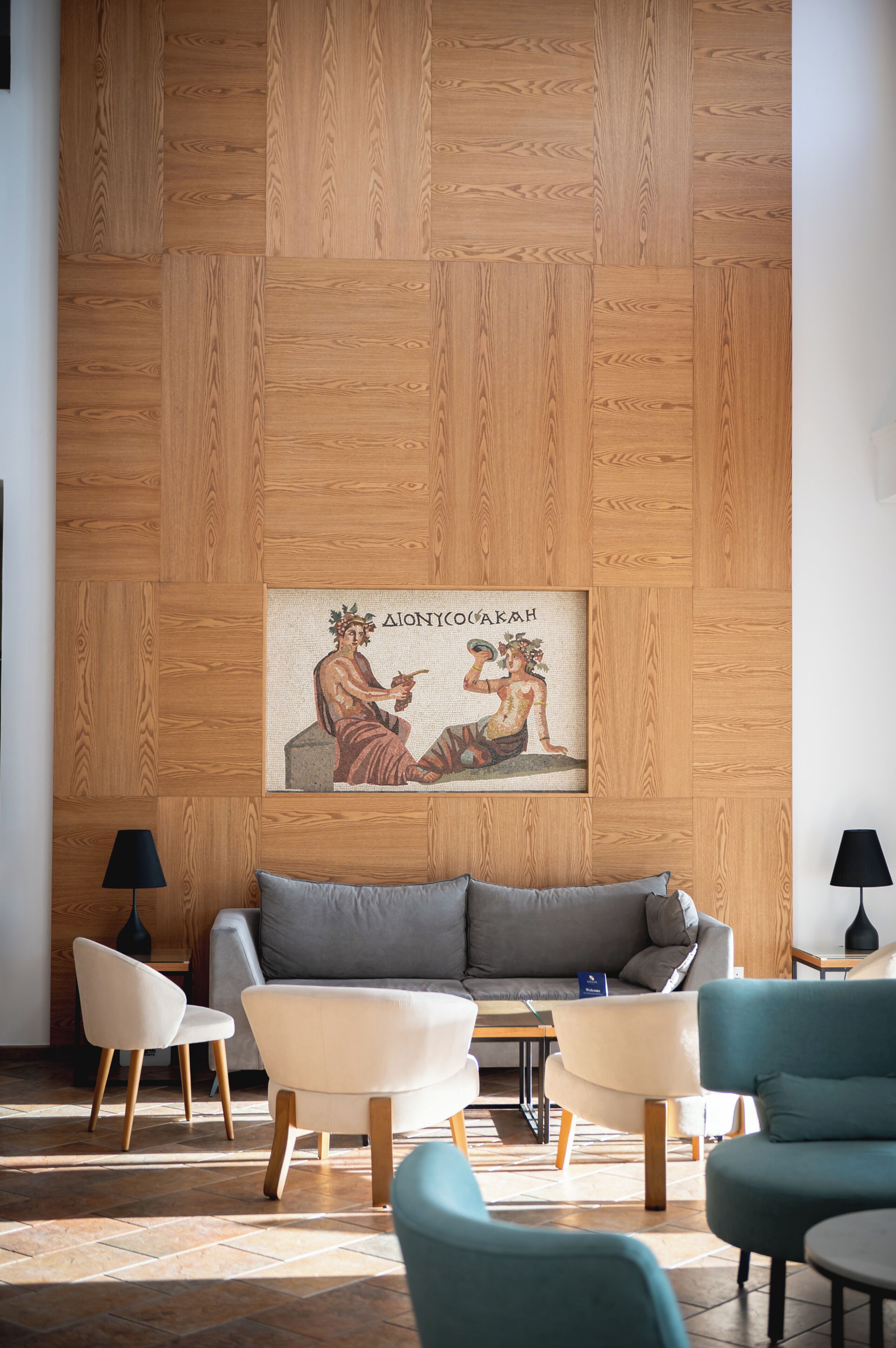Quarto com parede de painel de madeira, um sofá cinza e cadeiras verde-água.
