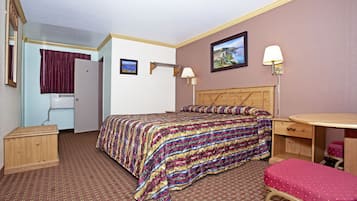 Quarto de hotel com cama, mesa de cabeceira, escrivaninha, cadeira e um pequeno armário de madeira.