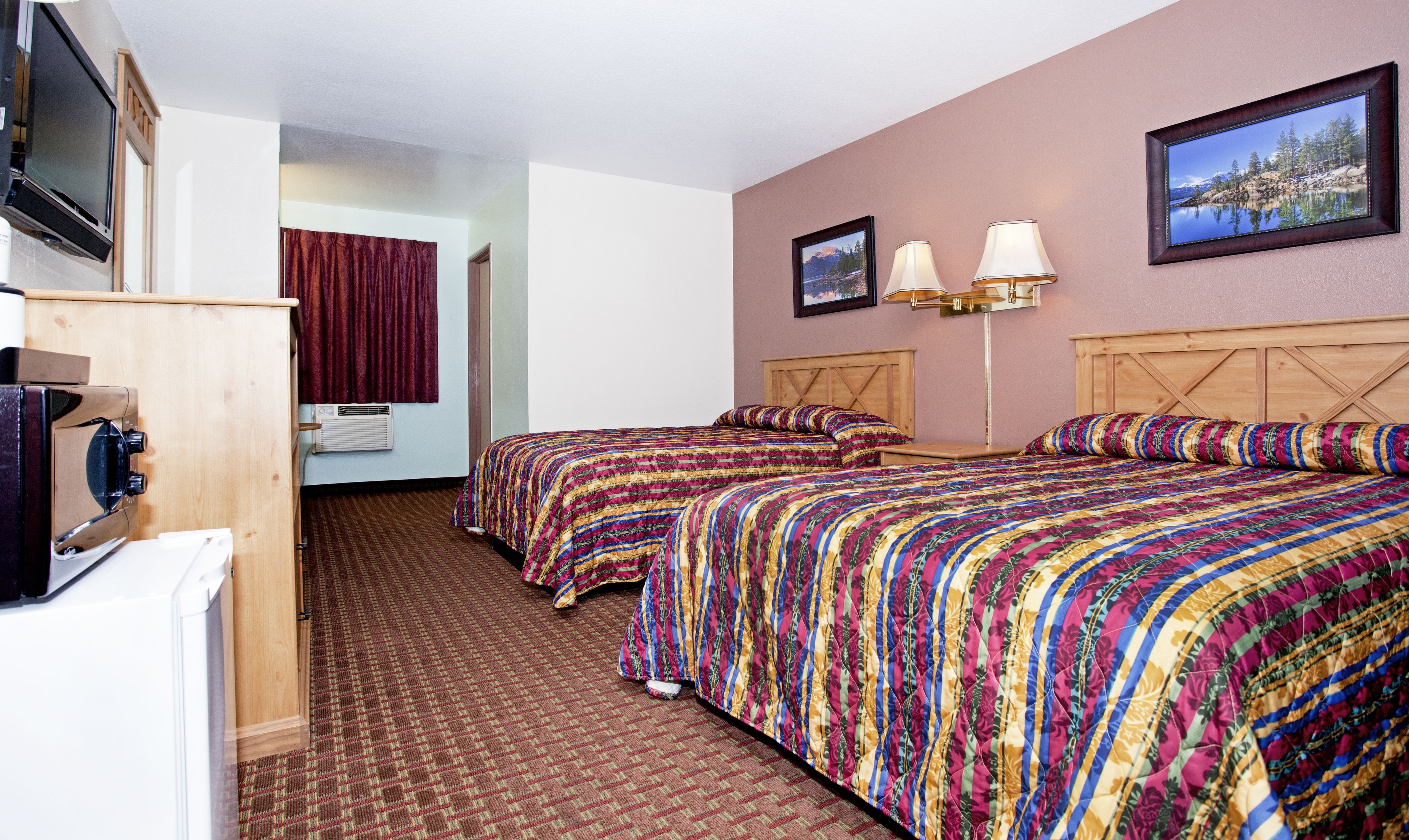 Quarto de hotel com duas camas, uma televisão, um quadro e um abajur.