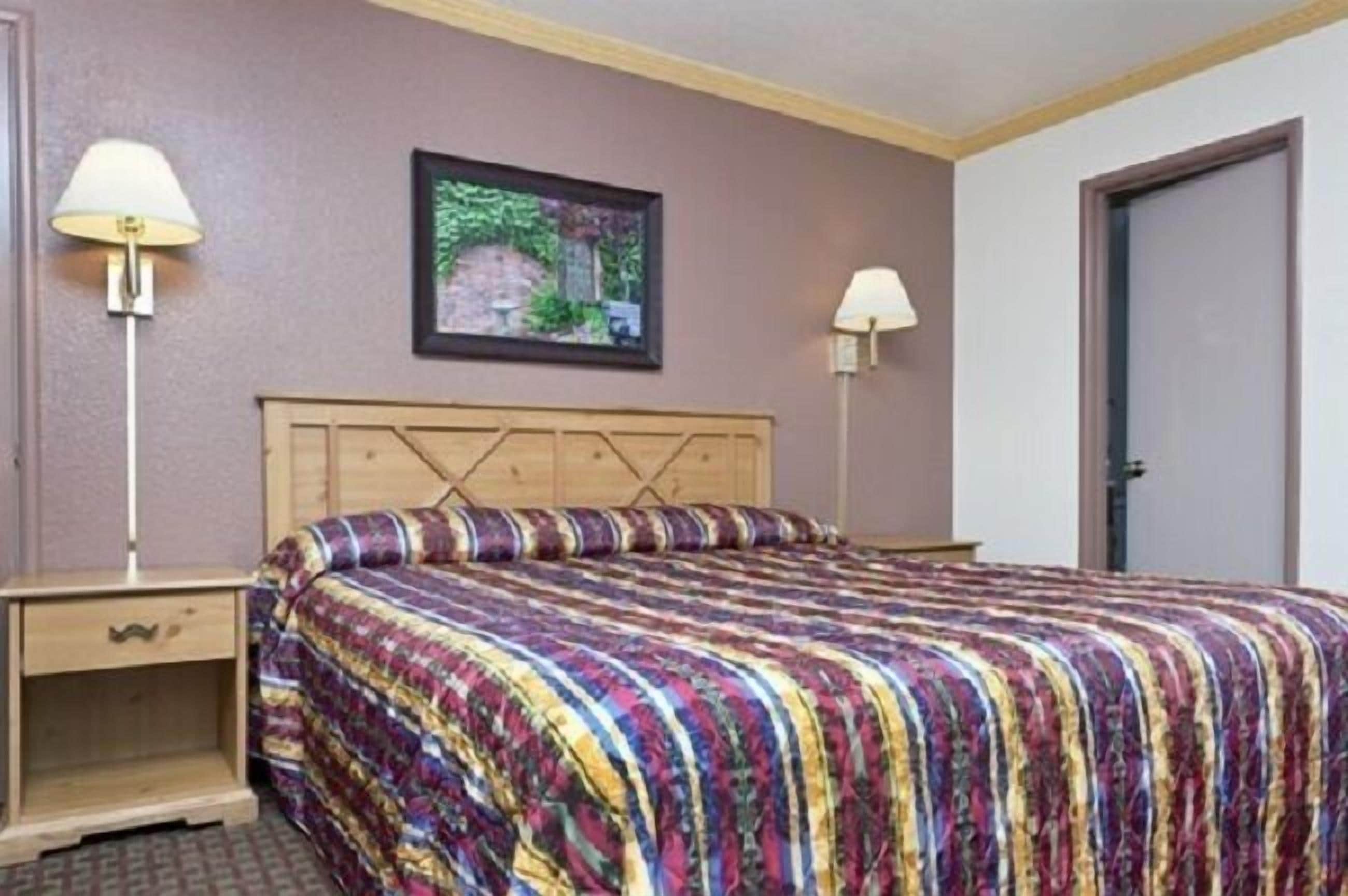 Um quarto com cabeceira de madeira, colcha listrada e colorida, duas luminárias de cabeceira e um quadro na parede.
