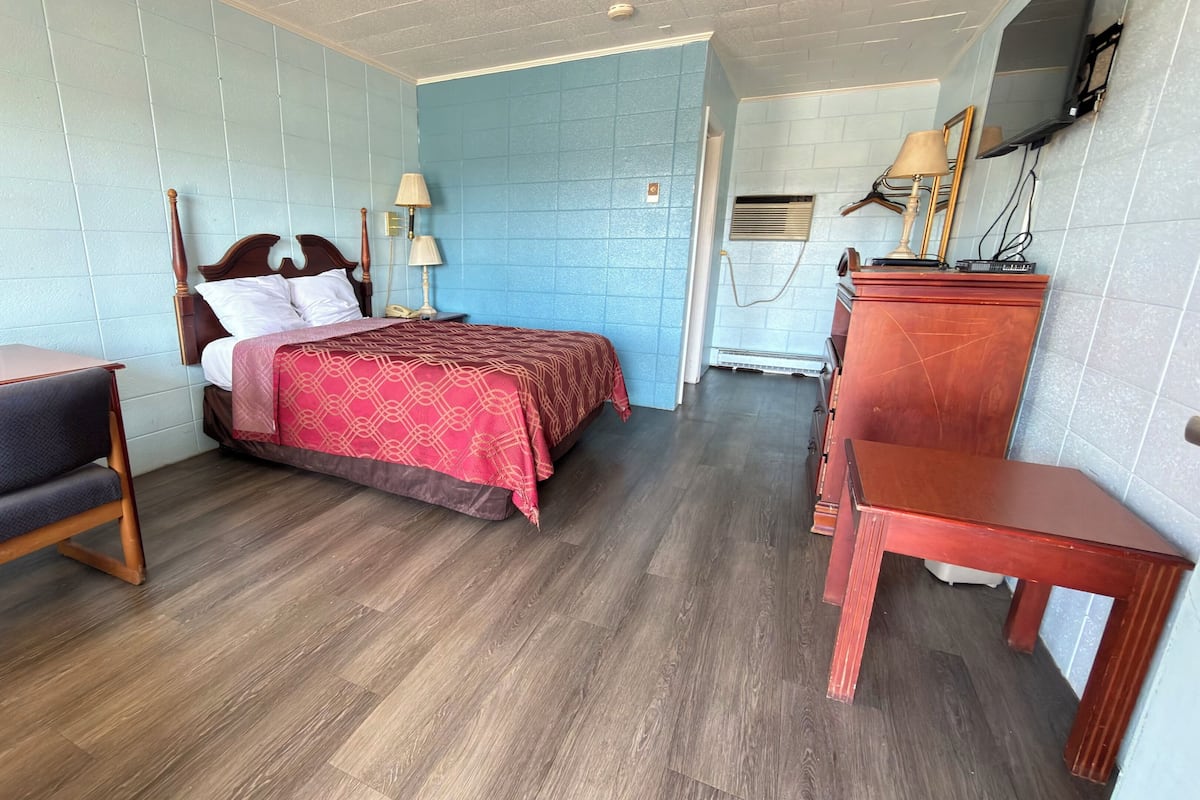 Quarto com cama, escrivaninha, cadeira, cômoda e televisão fixada na parede.
